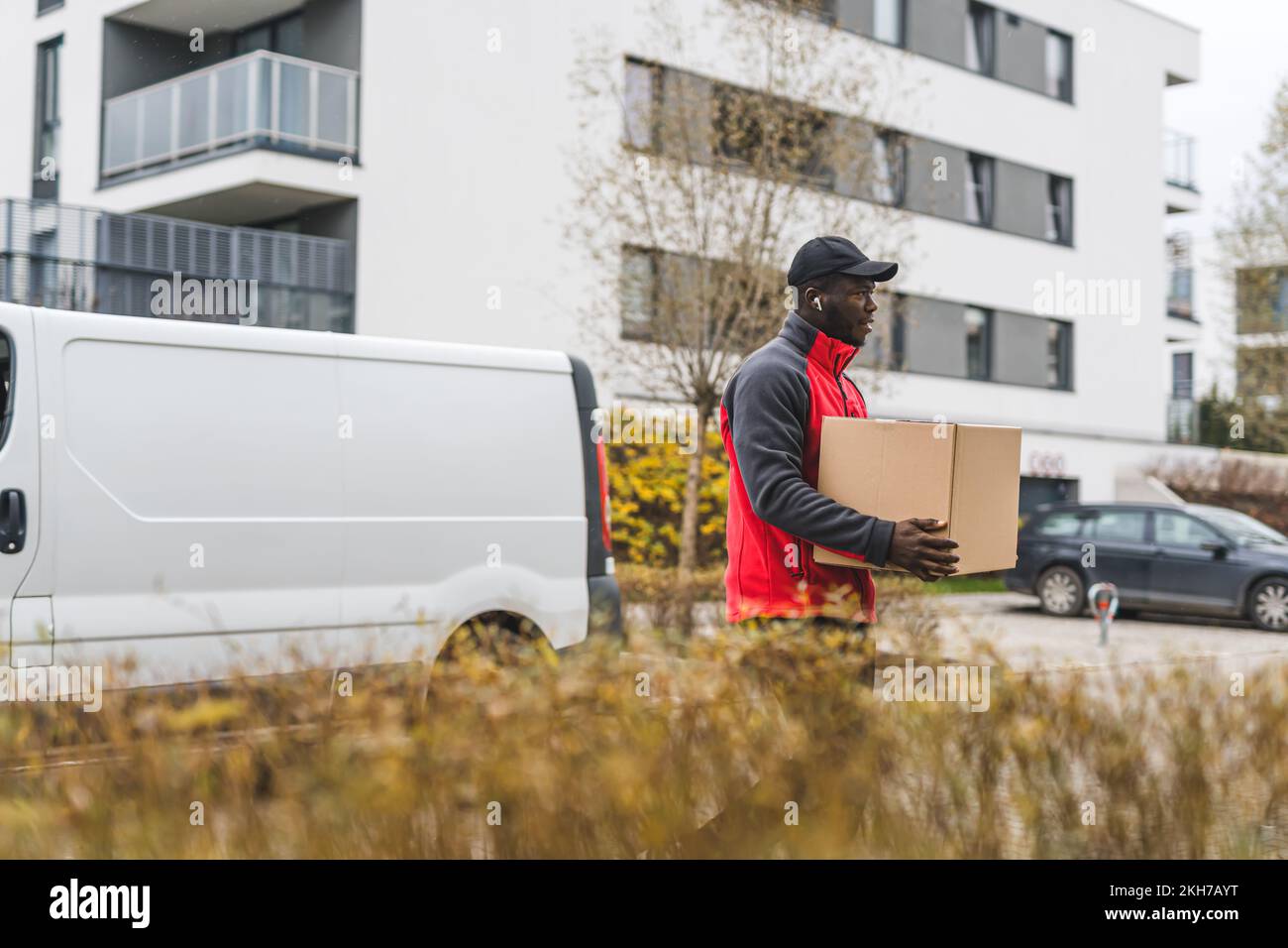 Black young adult delivery man carrying carboard box parcel unloaded ...