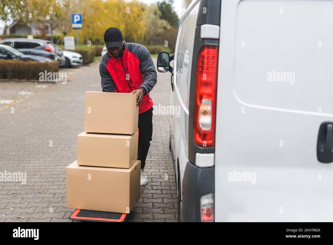 Black young adult delivery man in work uniform unloading carboard box ...