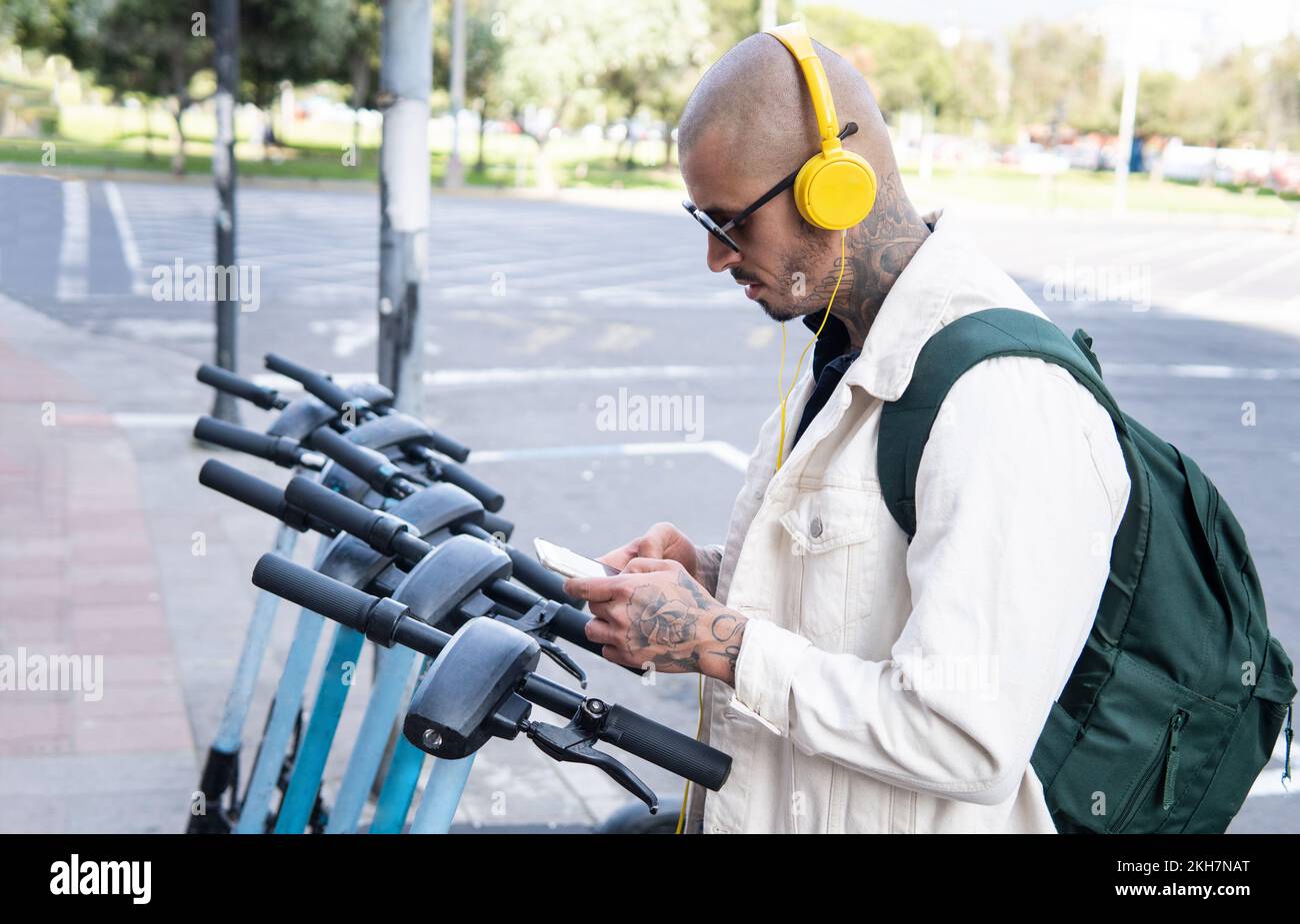 Bald young man with yellow headphones using a cell phone app to ride a ...