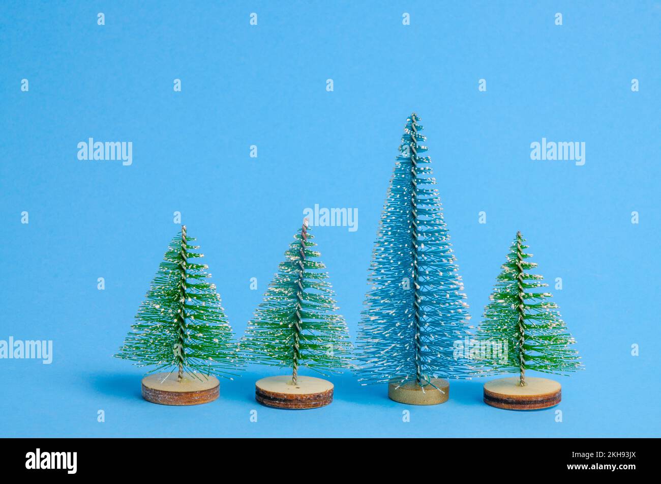 Four Blue And Green Artificial Christmas Trees On Blue Background With Copy Space Christmas