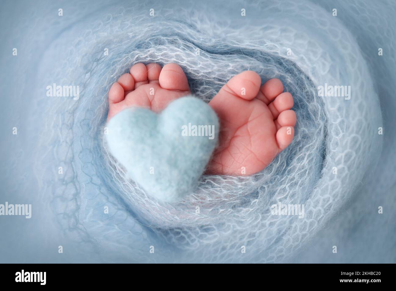 Legs, toes, foot and heels of a newborn. Knitted blue heart in baby's ...
