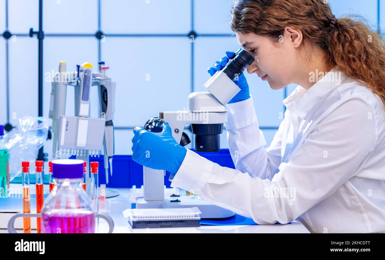 young adult female student working with a microscope examining ...
