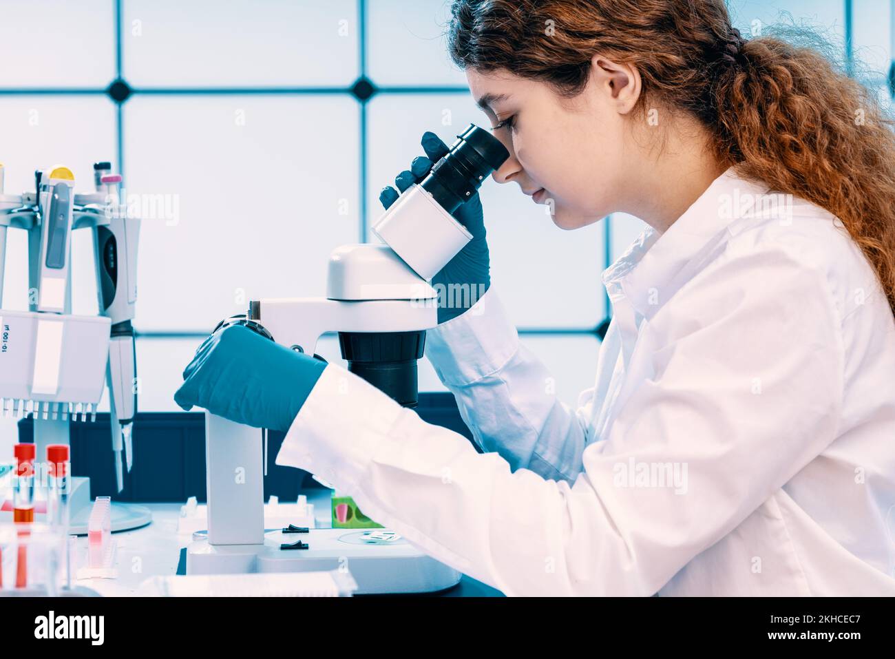 young adult female student working with a microscope examining ...