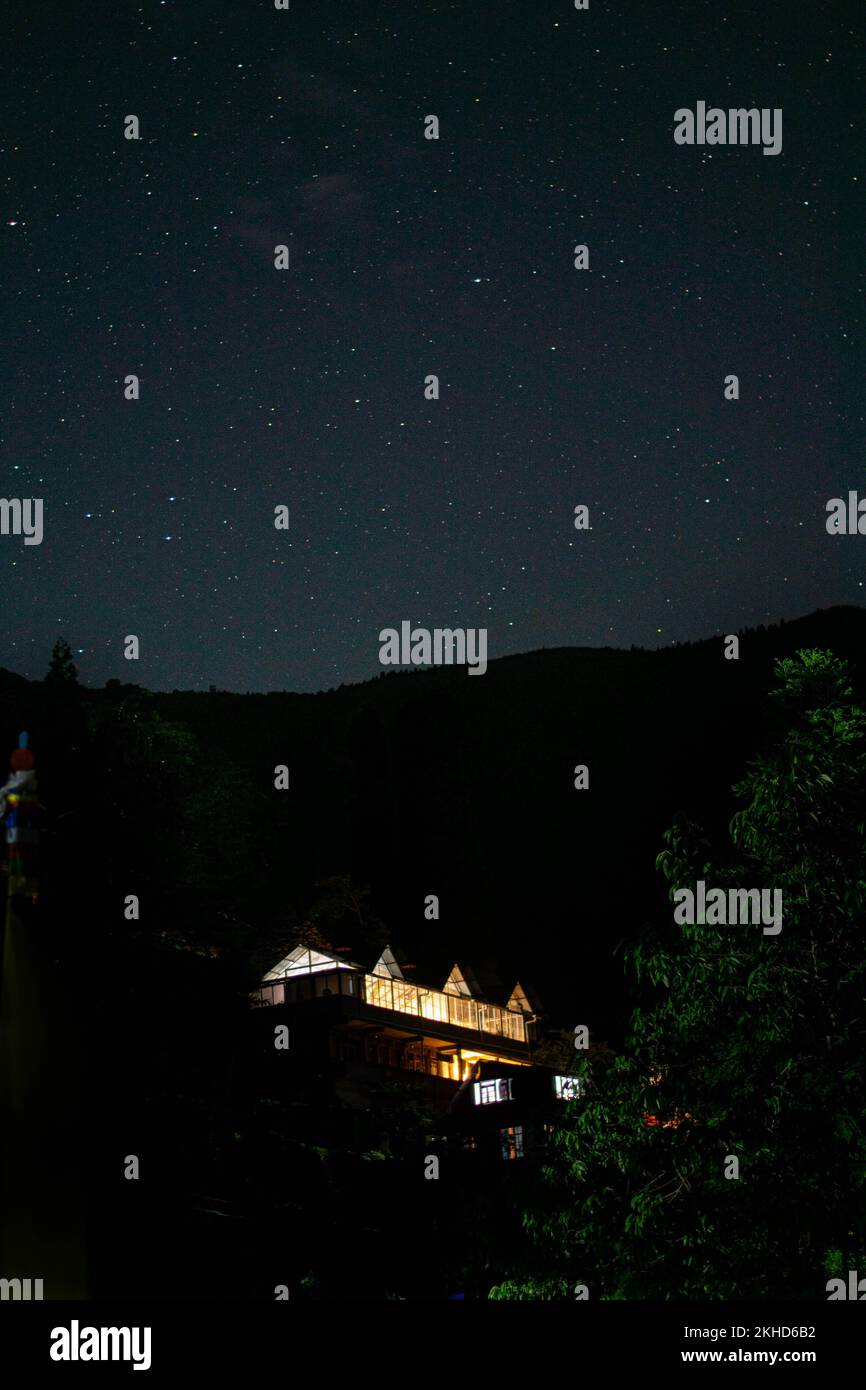 A house with bright lights in the forest with a starry night background ...