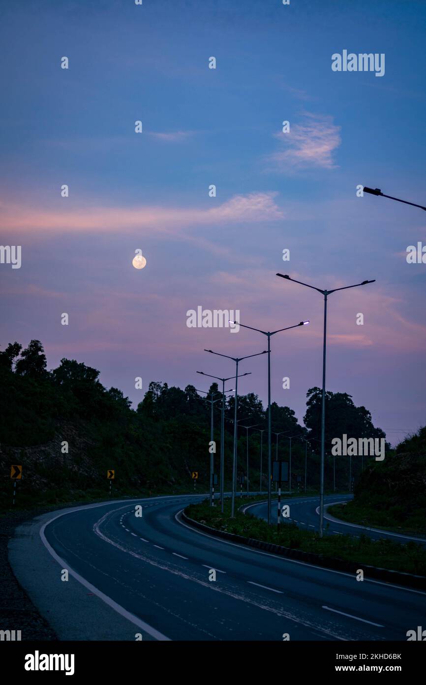 A curved highway road with street lights and a full mon in the sky ...