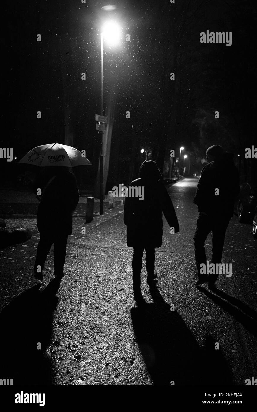 three people walk in the rain at night Stock Photo - Alamy