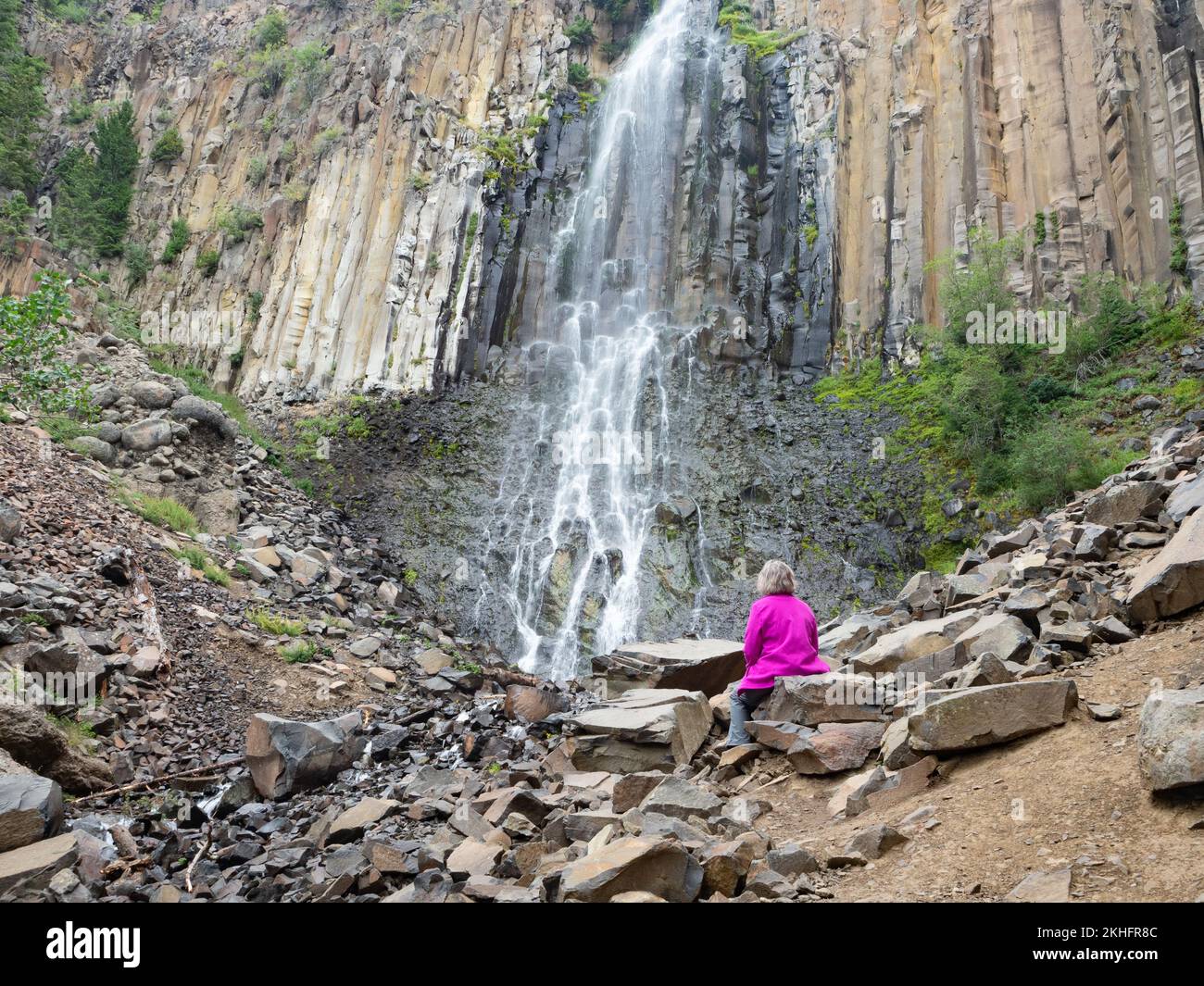 Senior adult woman wearing pink jacket and gray pants sitting on a ...
