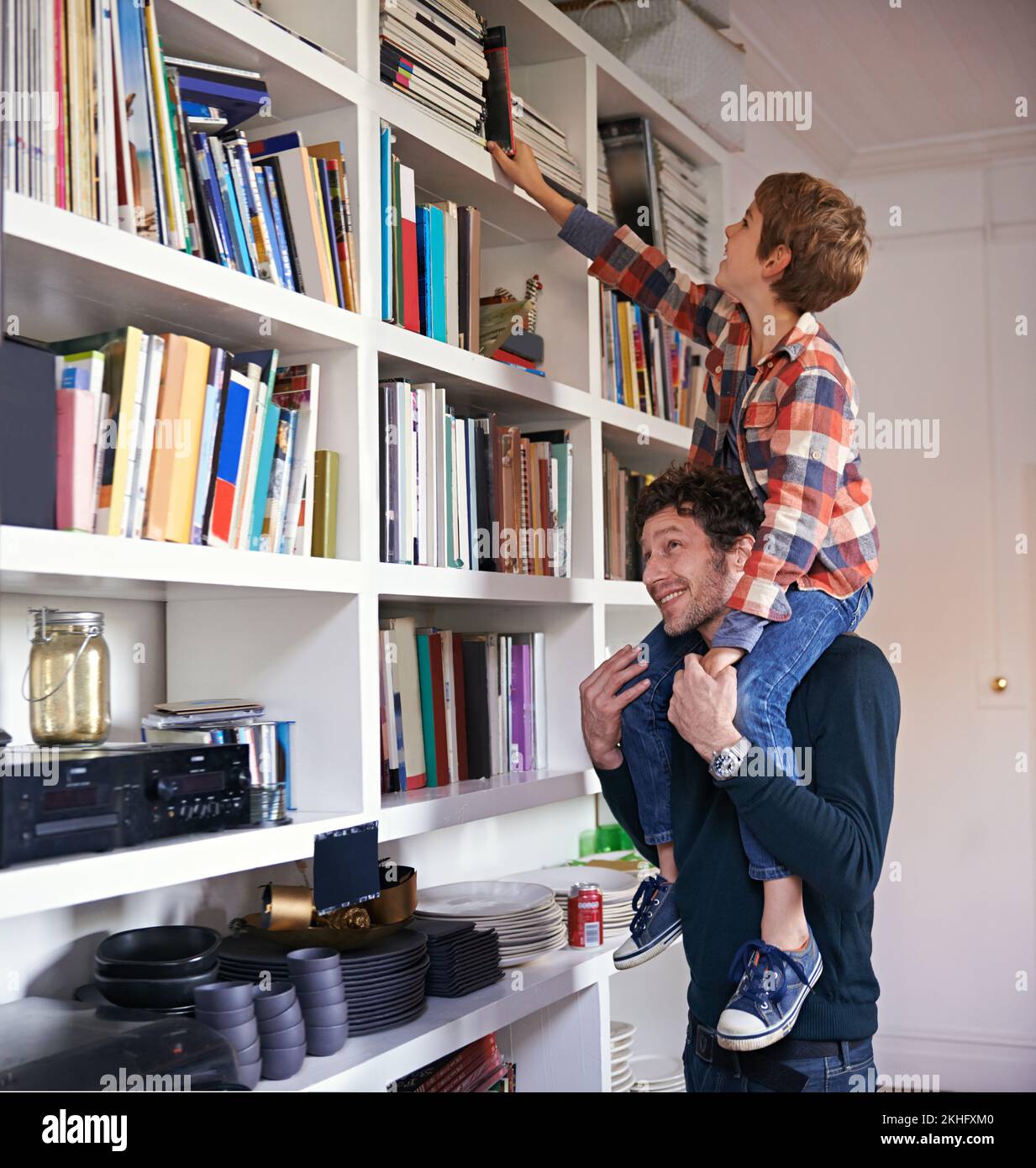 Reaching for a beloved book. A young boy sitting on his dads shoulders ...