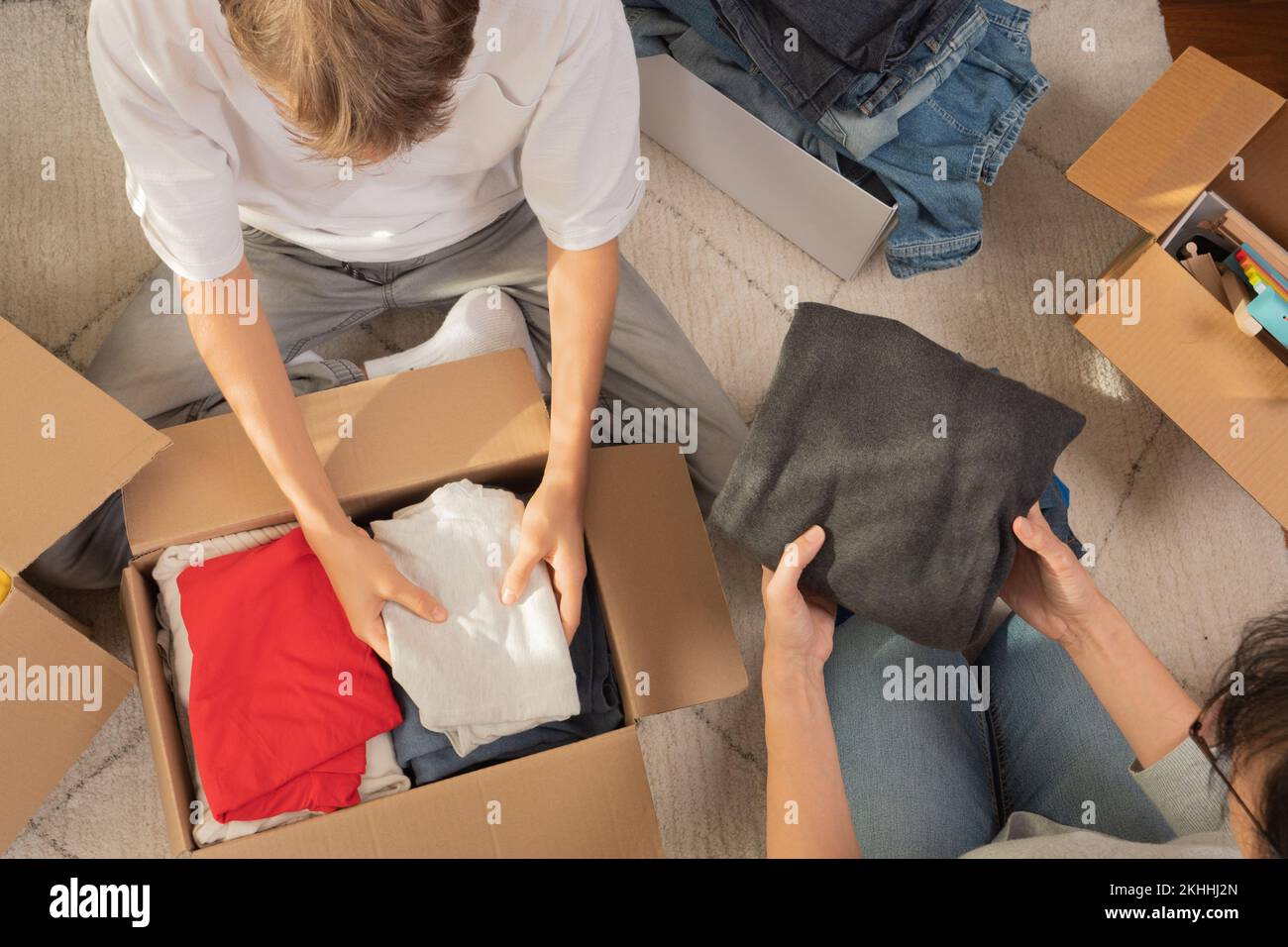 Woman and child sorting clothes and packing into cardboard box ...