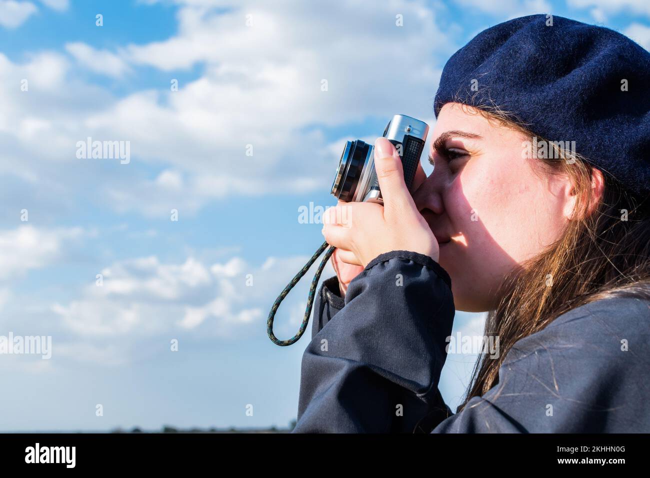 A pretty young woman with a blue beret hat photographing with a camera ...