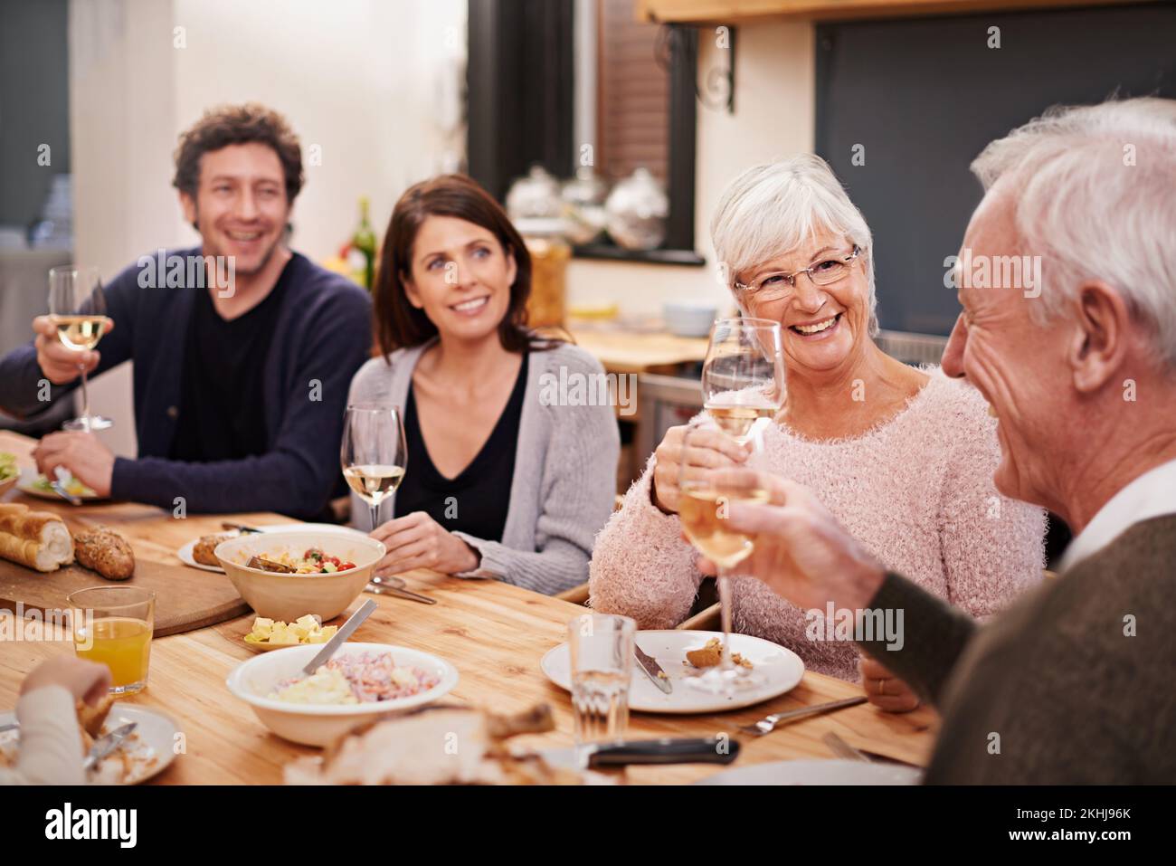 Raising a glass. a family sitting down to dinner Stock Photo - Alamy