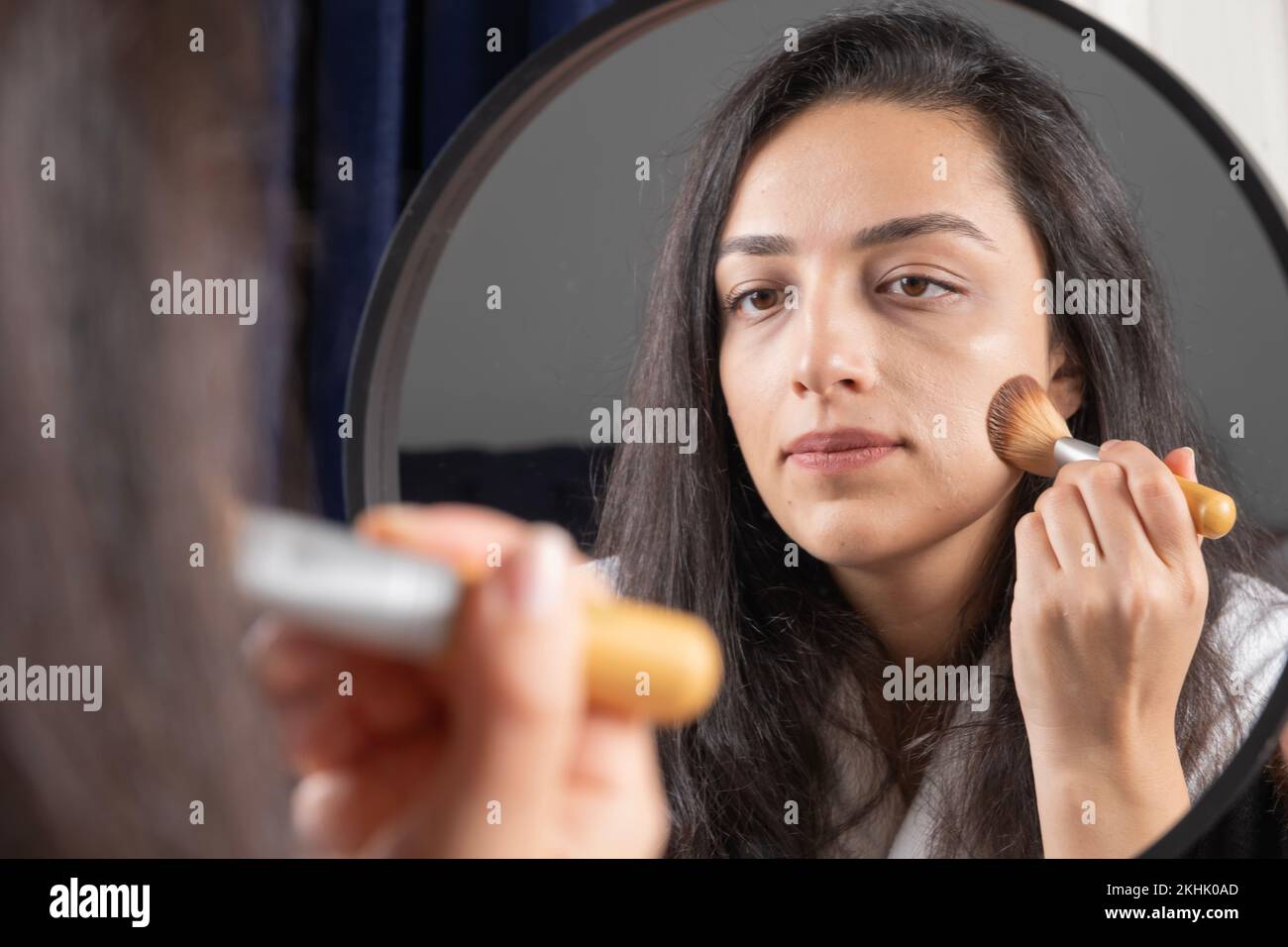 Young beautiful woman applying liquid foundation on her face with brush ...