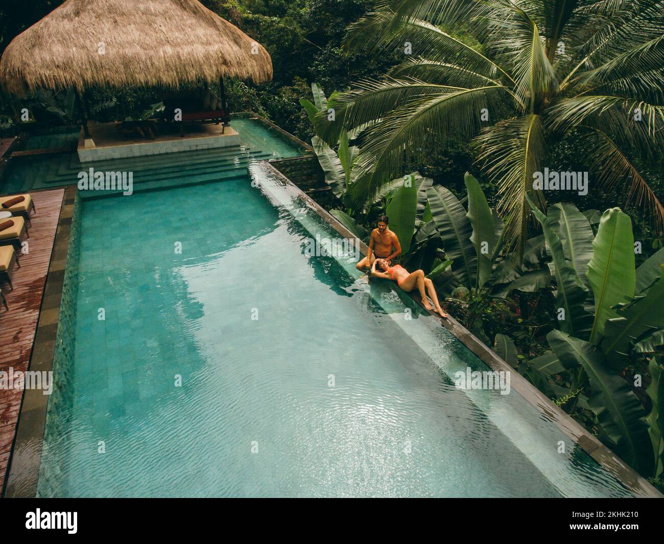Aerial shot of man and woman relaxing at the poolside. Couple enjoying ...