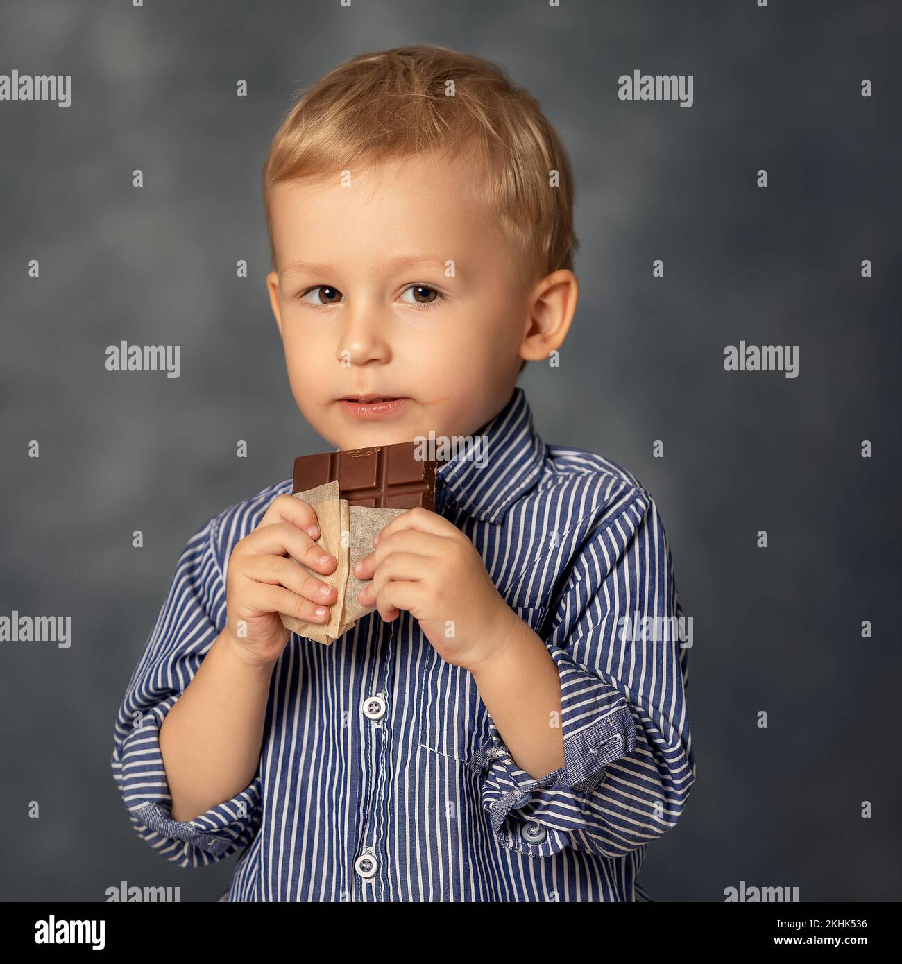 Portrait of small boy kid eating chocolate on grey background. Happy ...