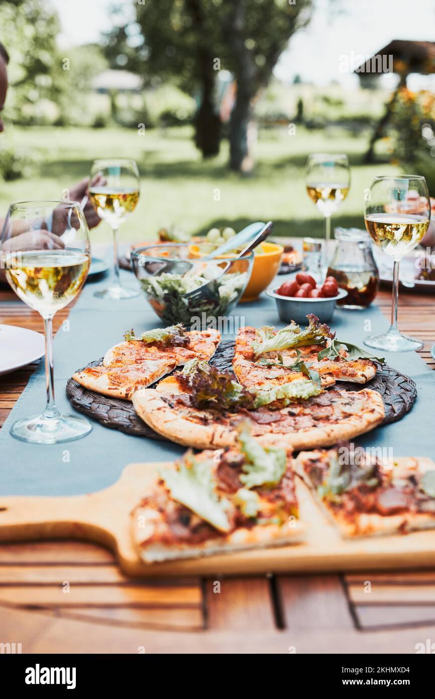 Dinner in a home garden. Pizza, salads, fruits and white wine on table ...