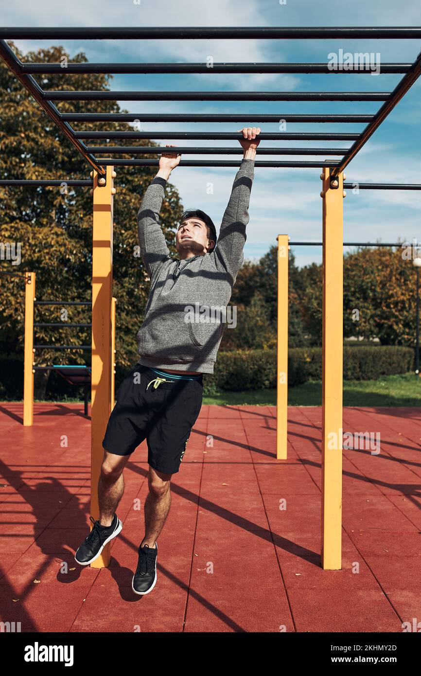 Young man bodybuilder exercising on monkey bars during his workout in a ...