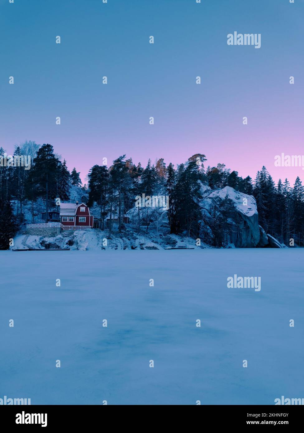 A vertical shot of a snow-covered field with spruces and a wooden home ...