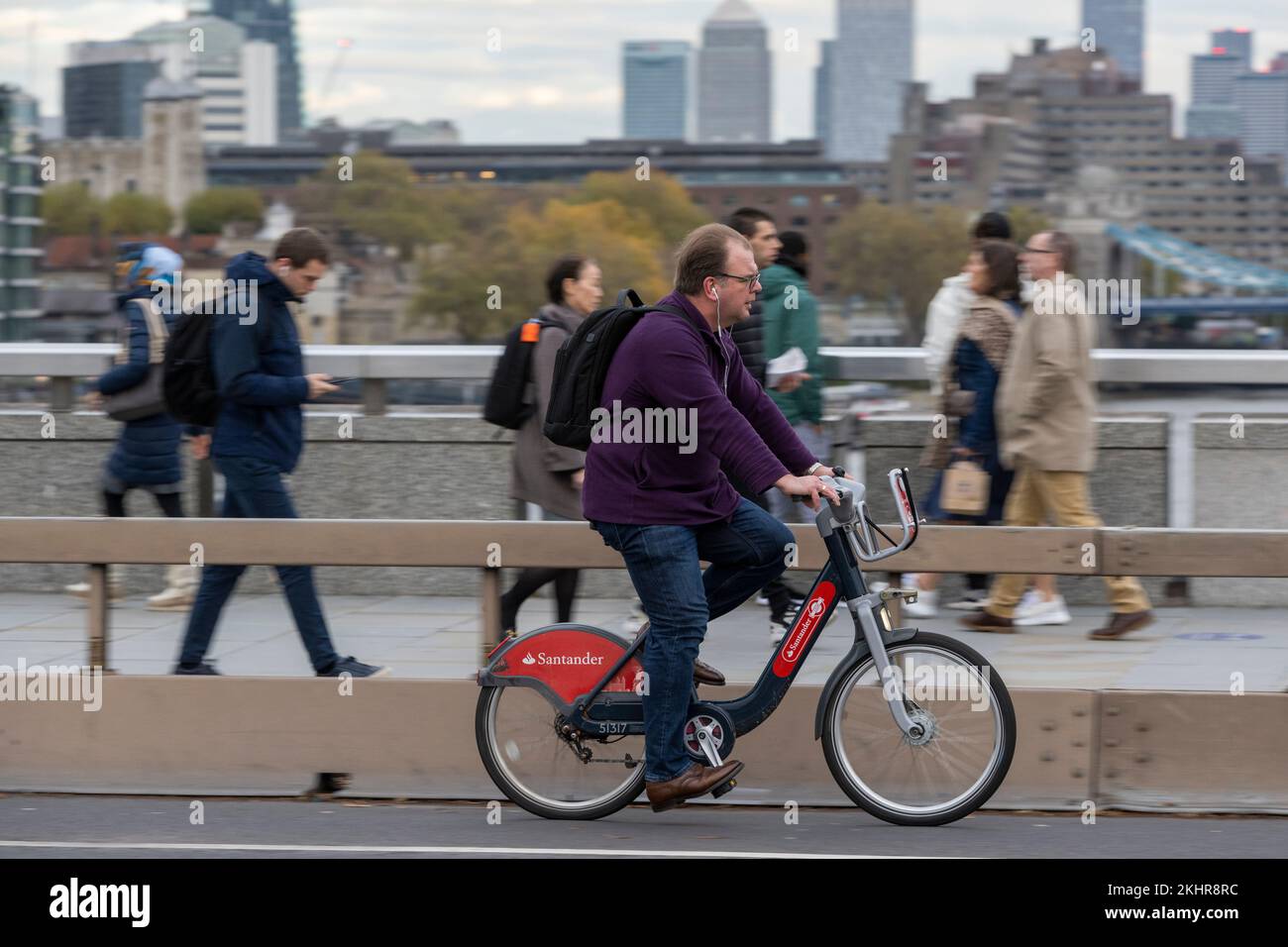 A man cycling during the rush hour, across London Bridge, on a Transport for London Santander ...