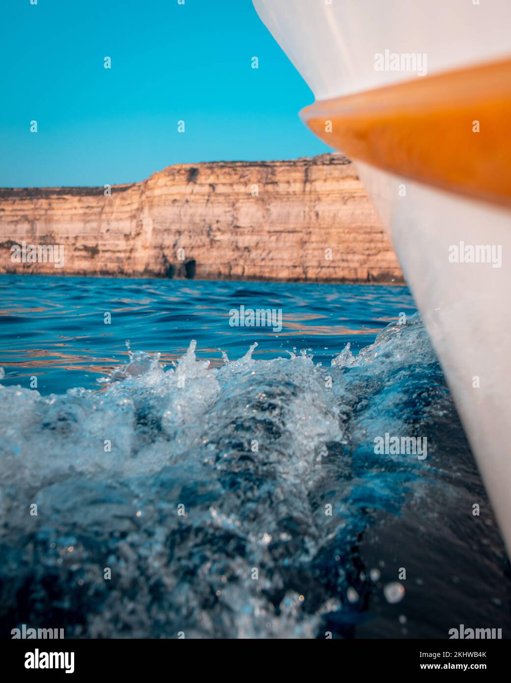 A vertical closeup of part of a boat making water waves sunlit rocky ...