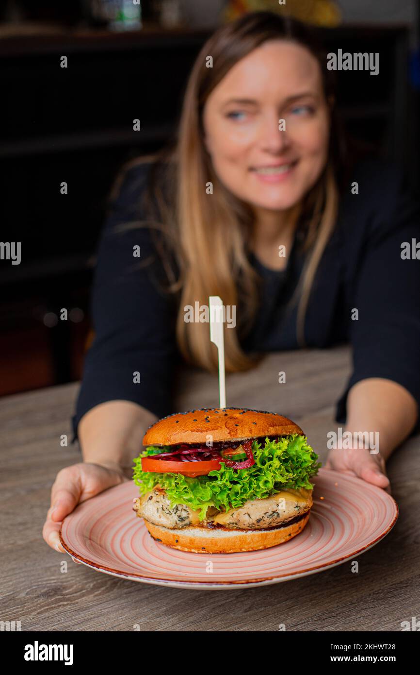 Vertical of blurred woman holding large double hamburger with skewer on ...