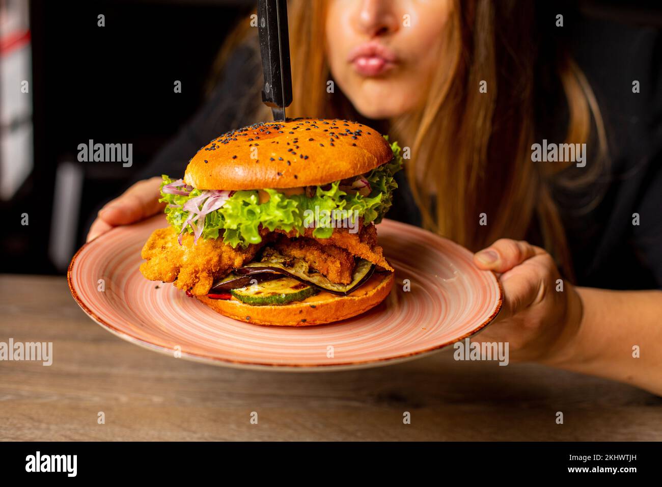 Cropped woman present and show double hamburger with knife in bun on ...