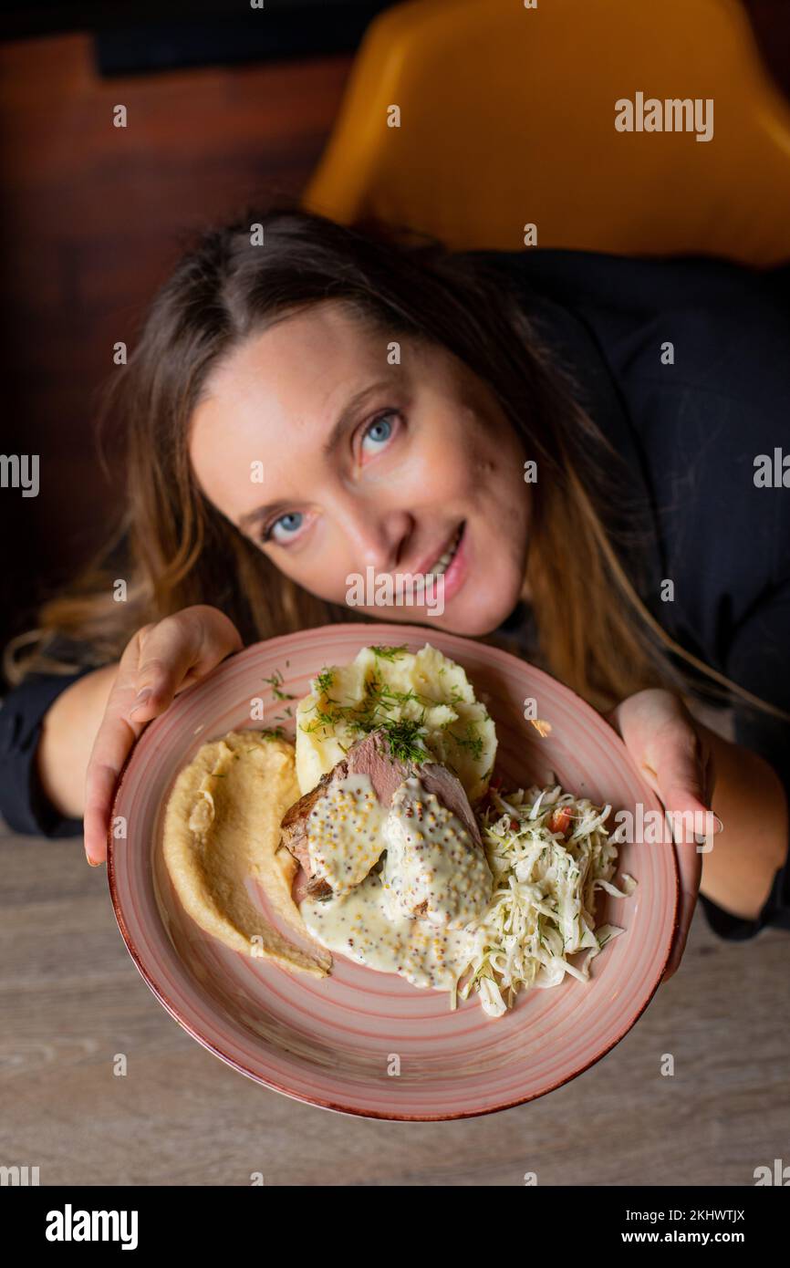 Vertical interested, smiling woman, chef holding and show plate of ...