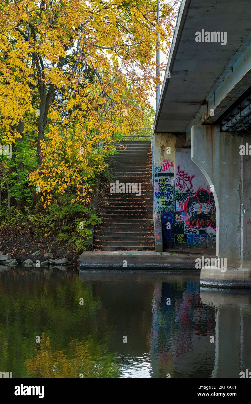 Colorful graffiti beneath a bridge next to a staircase and a river ...