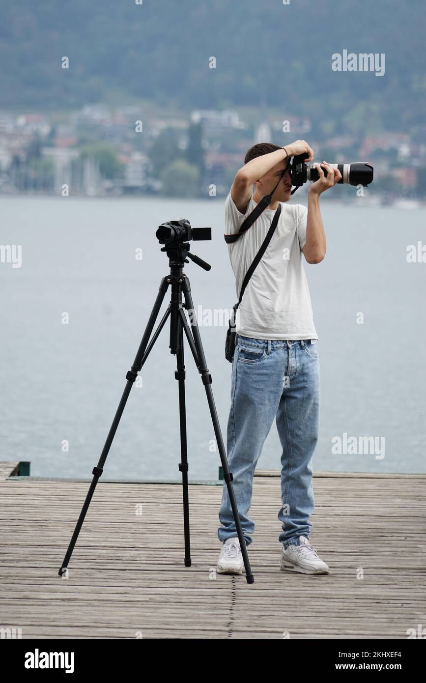 A vertical of a Caucasian young photographer with a video camera on the ...