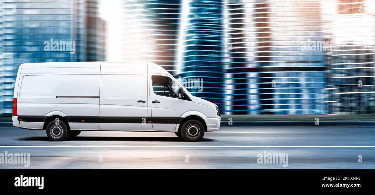 Van driving on a city road at sunset in front of a modern cityscape ...