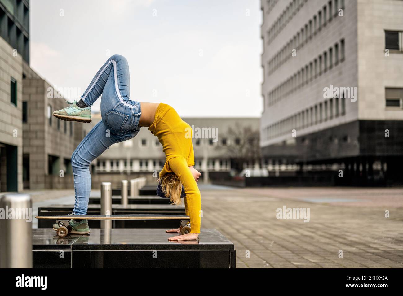 Athetic young woman in gymnastic pose with a skateboard, cityscape ...
