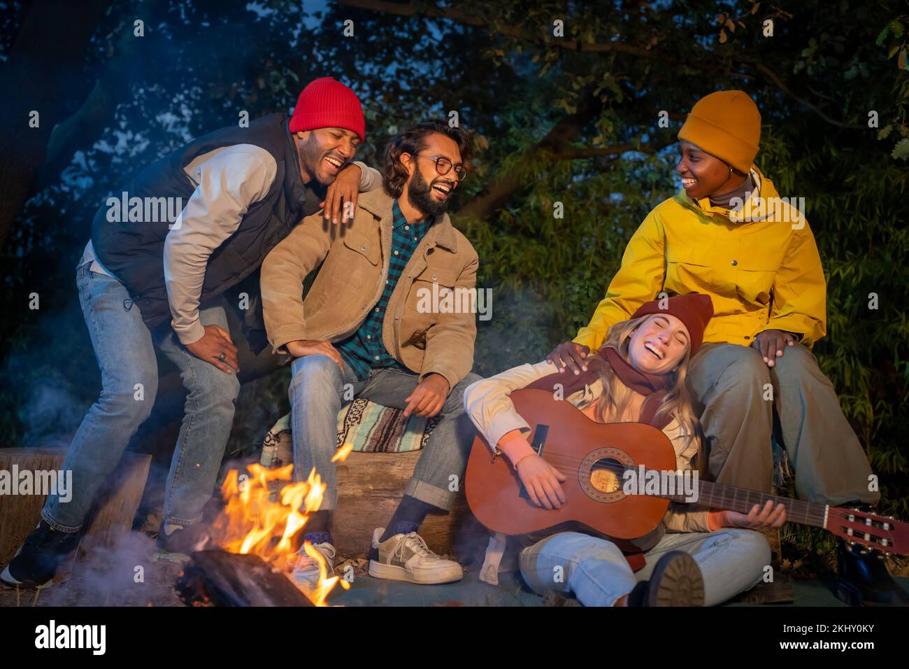 Happy multiracial friends at campsite laughing playing the guitar at ...