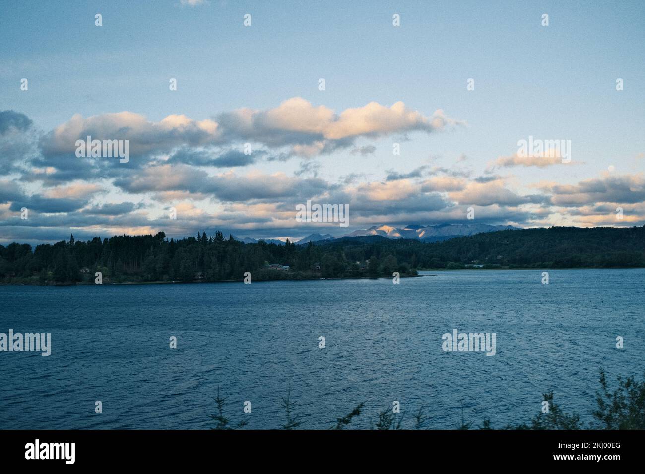 The view of the clouds floating above the smooth lake and shore with ...
