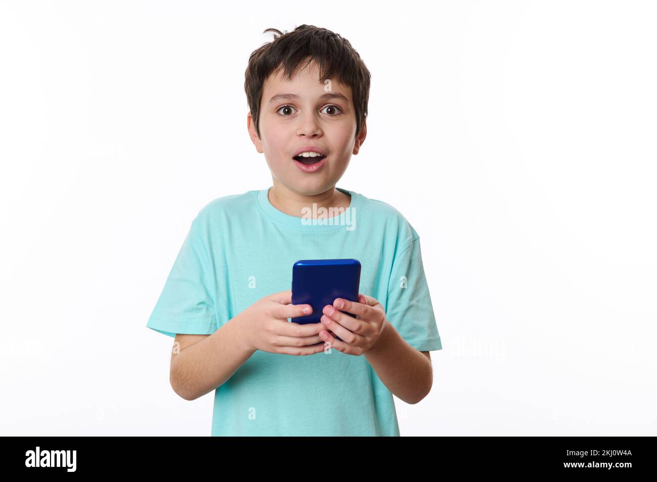 Amazed cute teenage boy, holding a cell phone and looking at camera ...