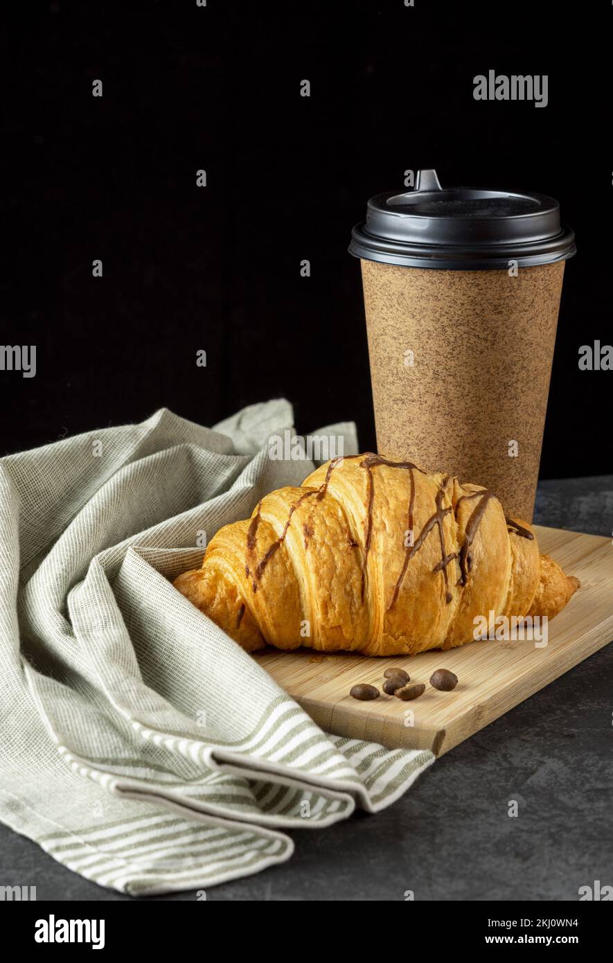 Paper cup with fragrant coffee and croissant on a dark background ...