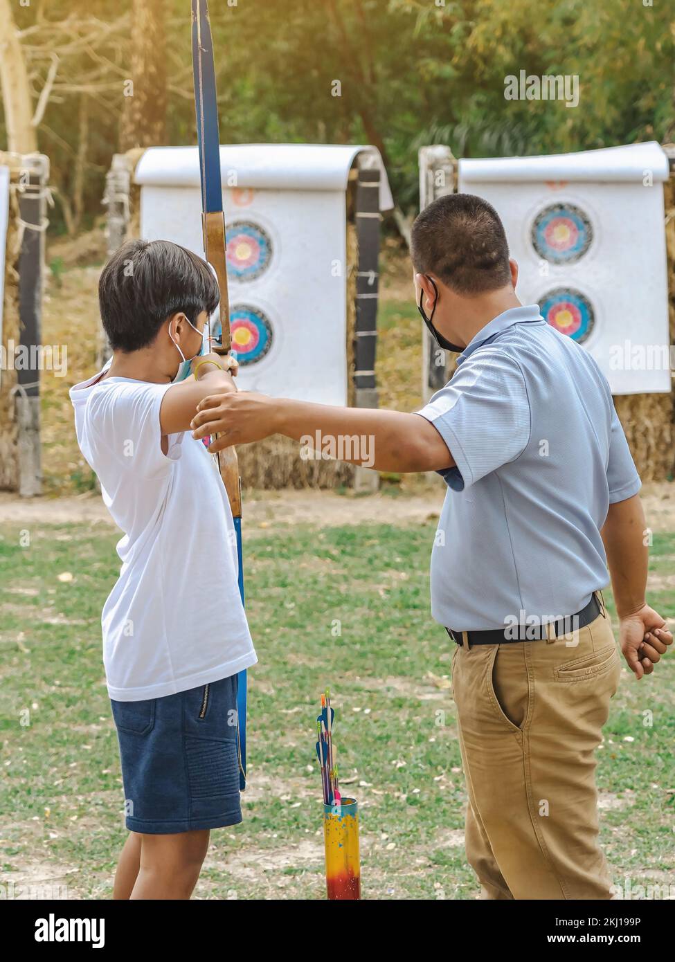 Back view of Asian boy wear face mask aims archery bow and arrow to ...