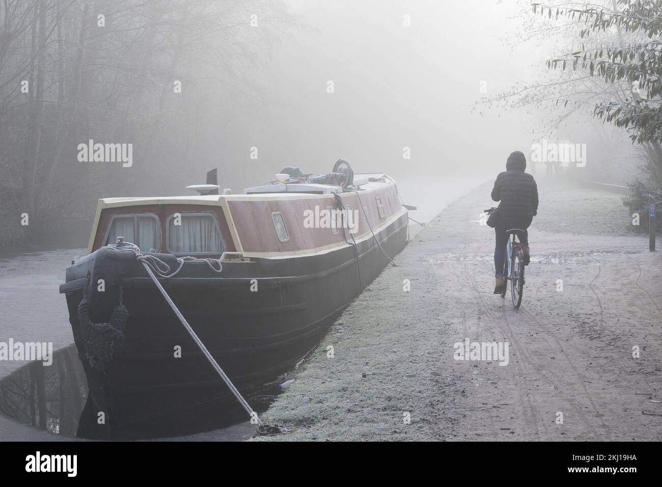 Frosty misty and frozen canal with a canal boat. A woman cycles along ...