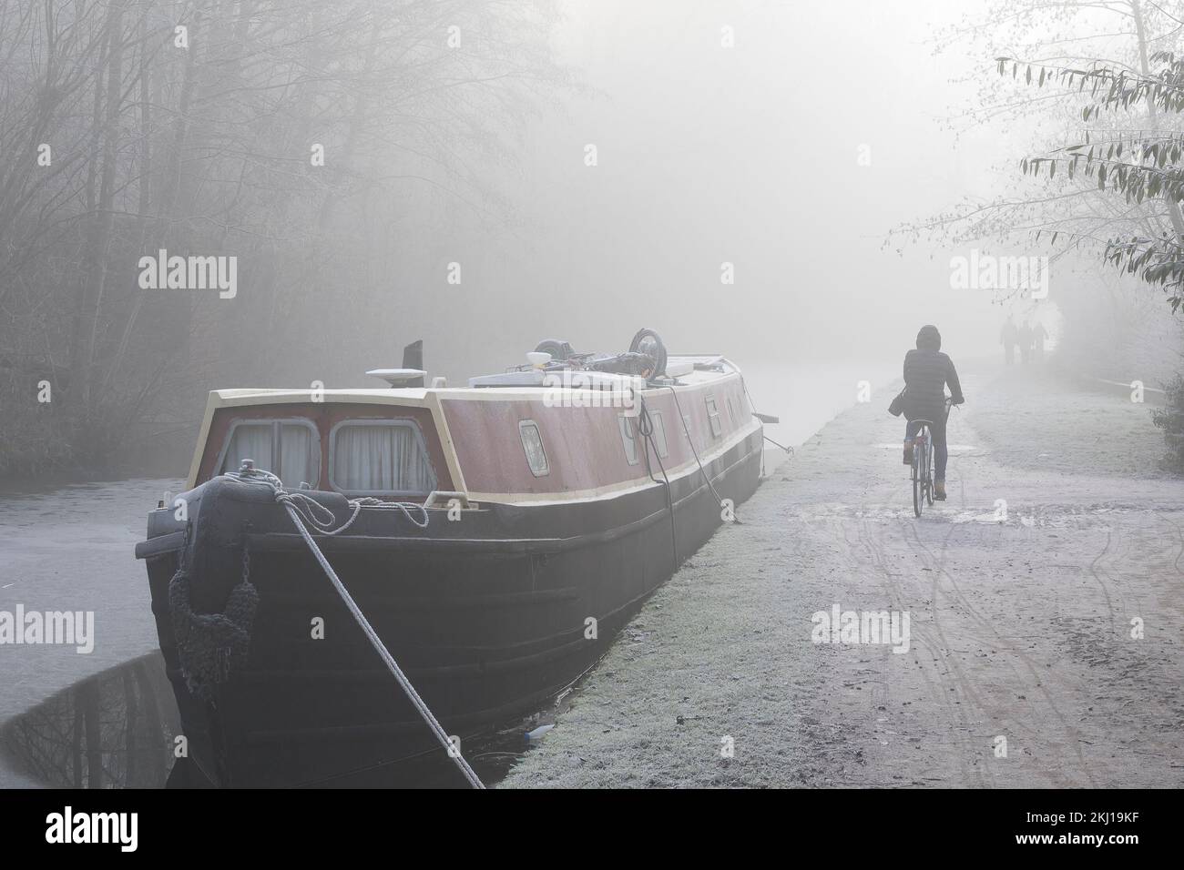 Frosty misty and frozen canal with a canal boat. A woman cycles along ...