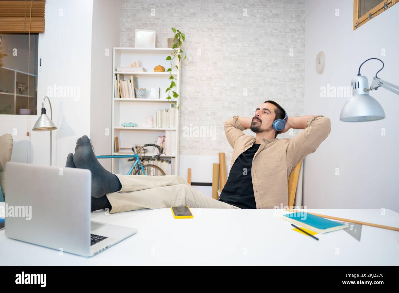 Positive young man keeping hands behind head while listening to music ...