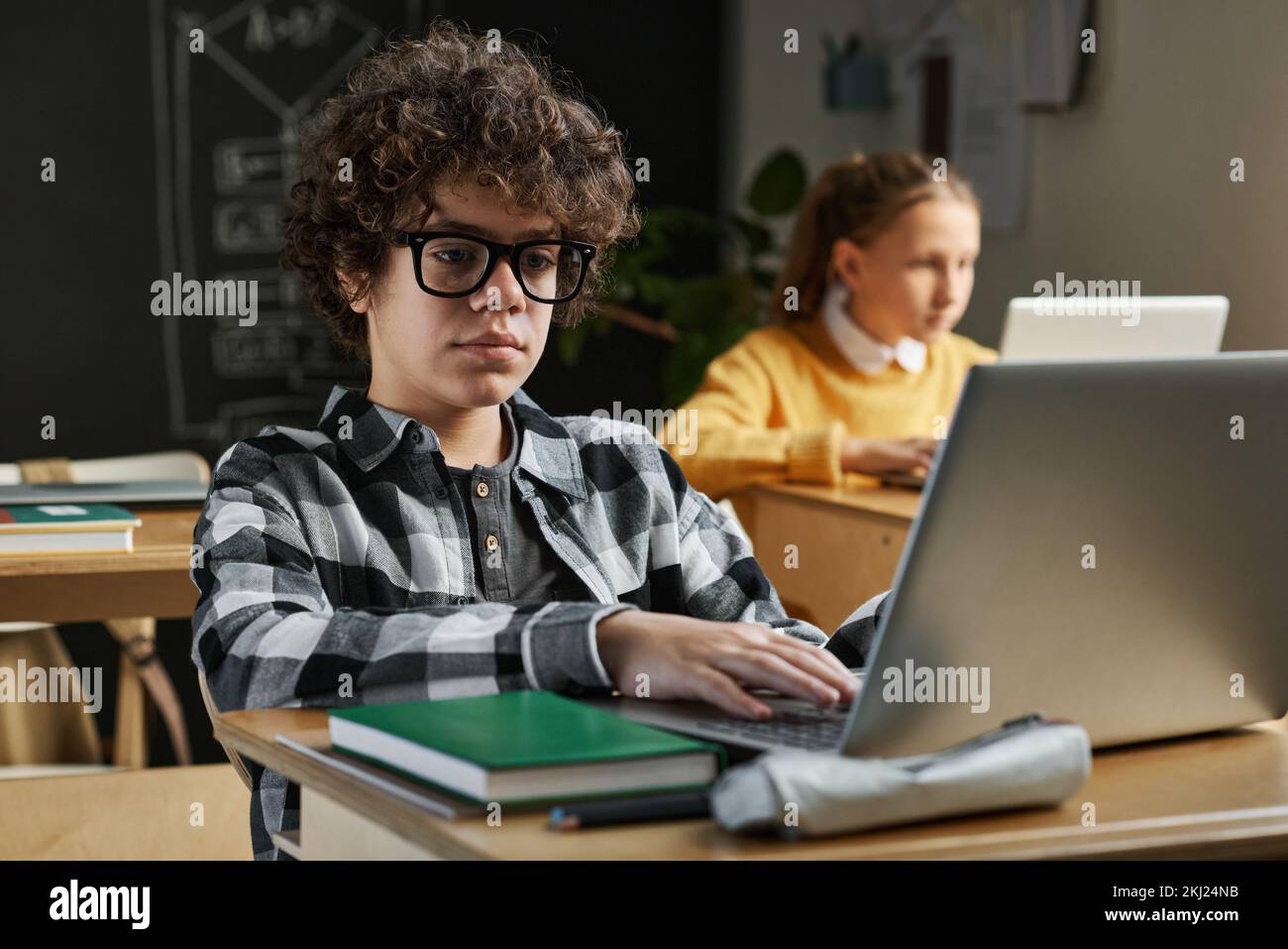 Schoolboy sitting at desk and typing on laptop, he learning to use ...