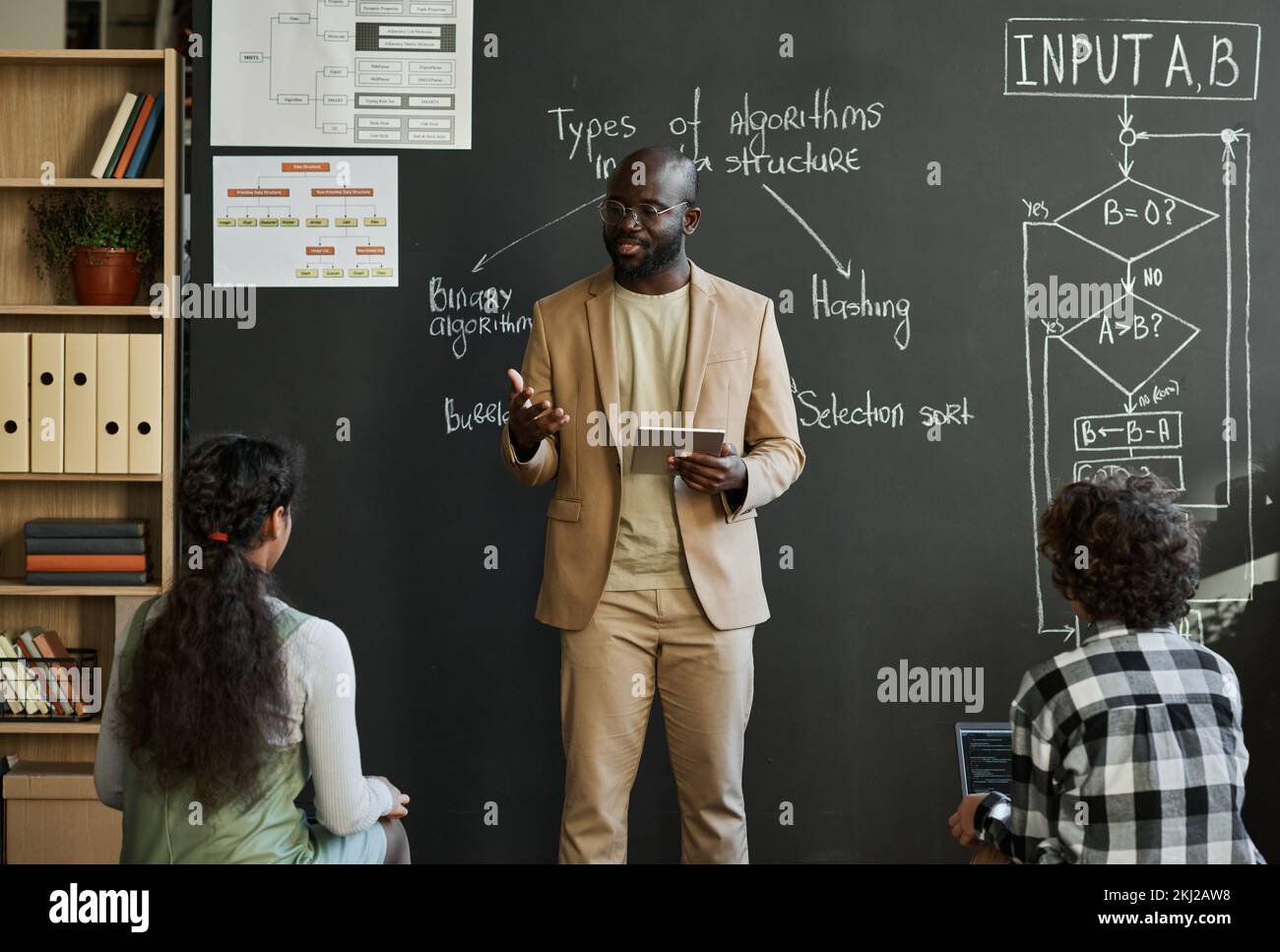 African American teacher standing near the blackboard with charts and ...
