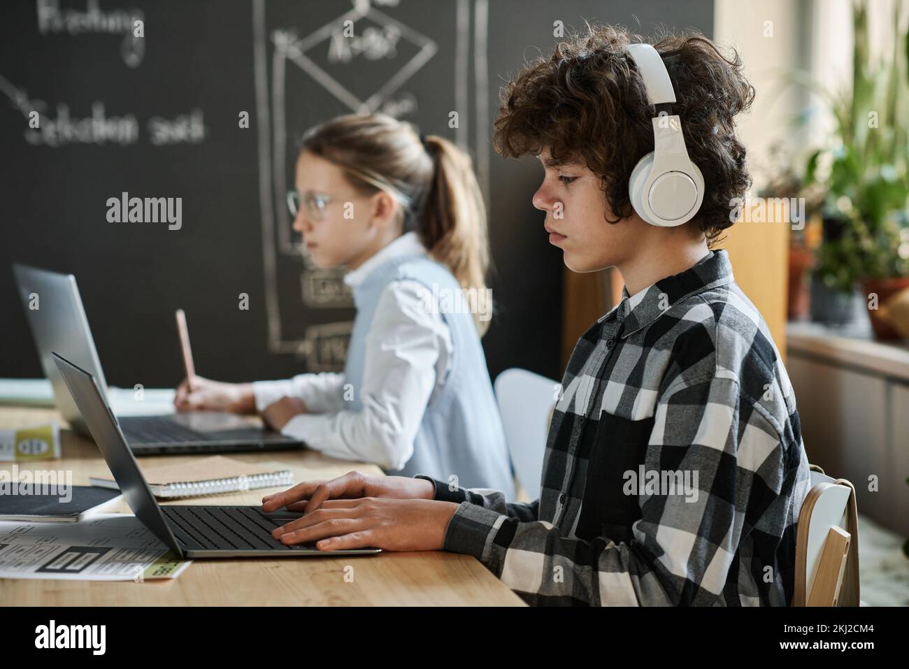 Boy in wireless headphones sitting at table and typing on laptop at IT ...