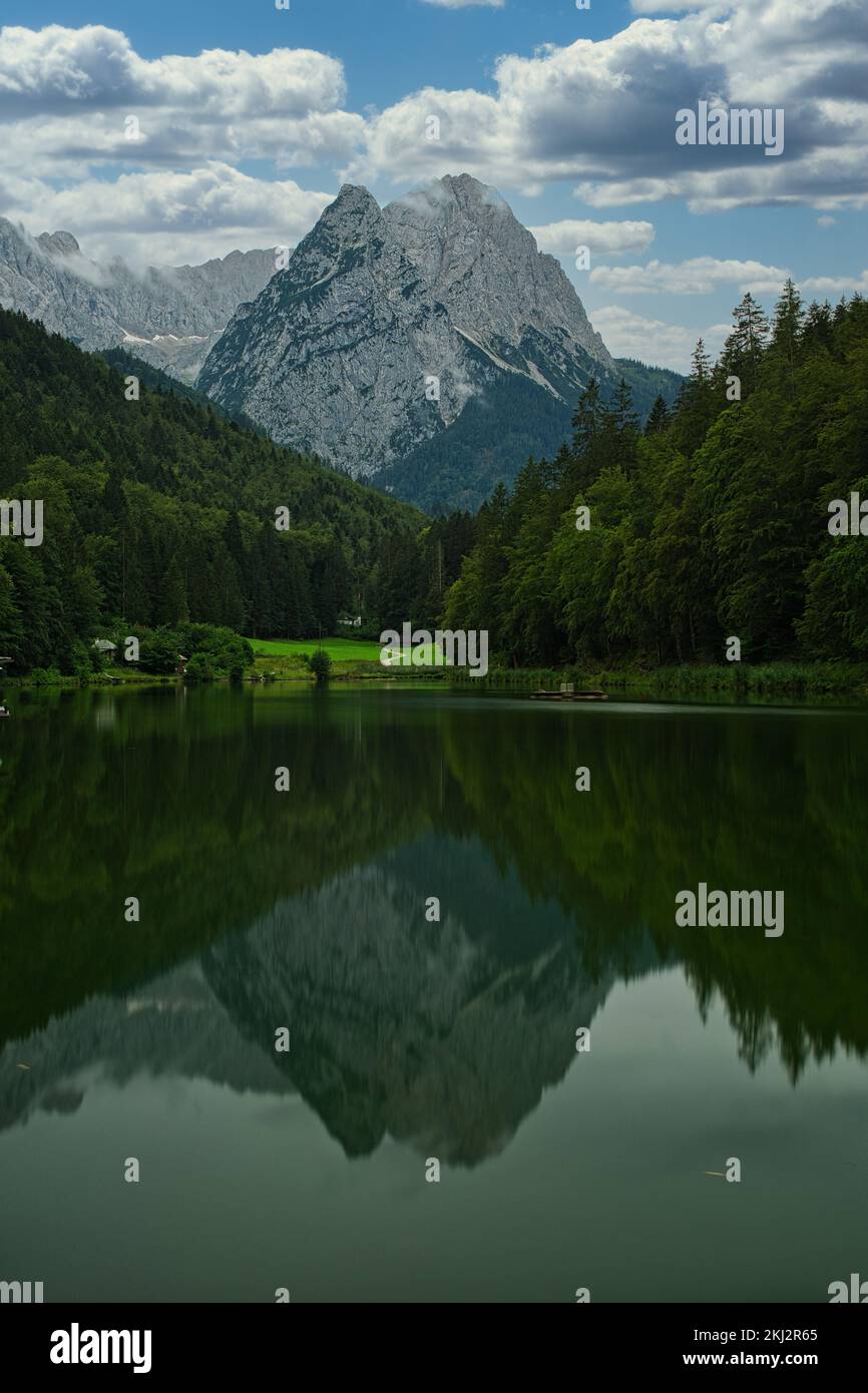 A vertical of the reflection of a snowy rocky mountain and green woods ...