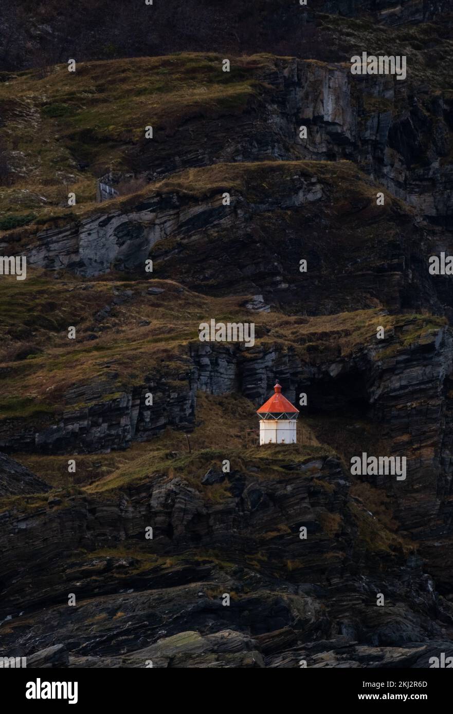 A vertical of a small lighthouse isolated on a green rocky mountain ...