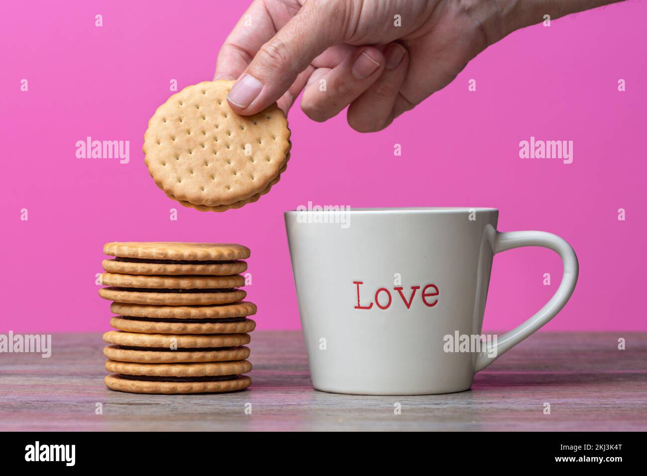 Hand taking a biscuit next to a mug with 'Love' written on it. Tea and ...