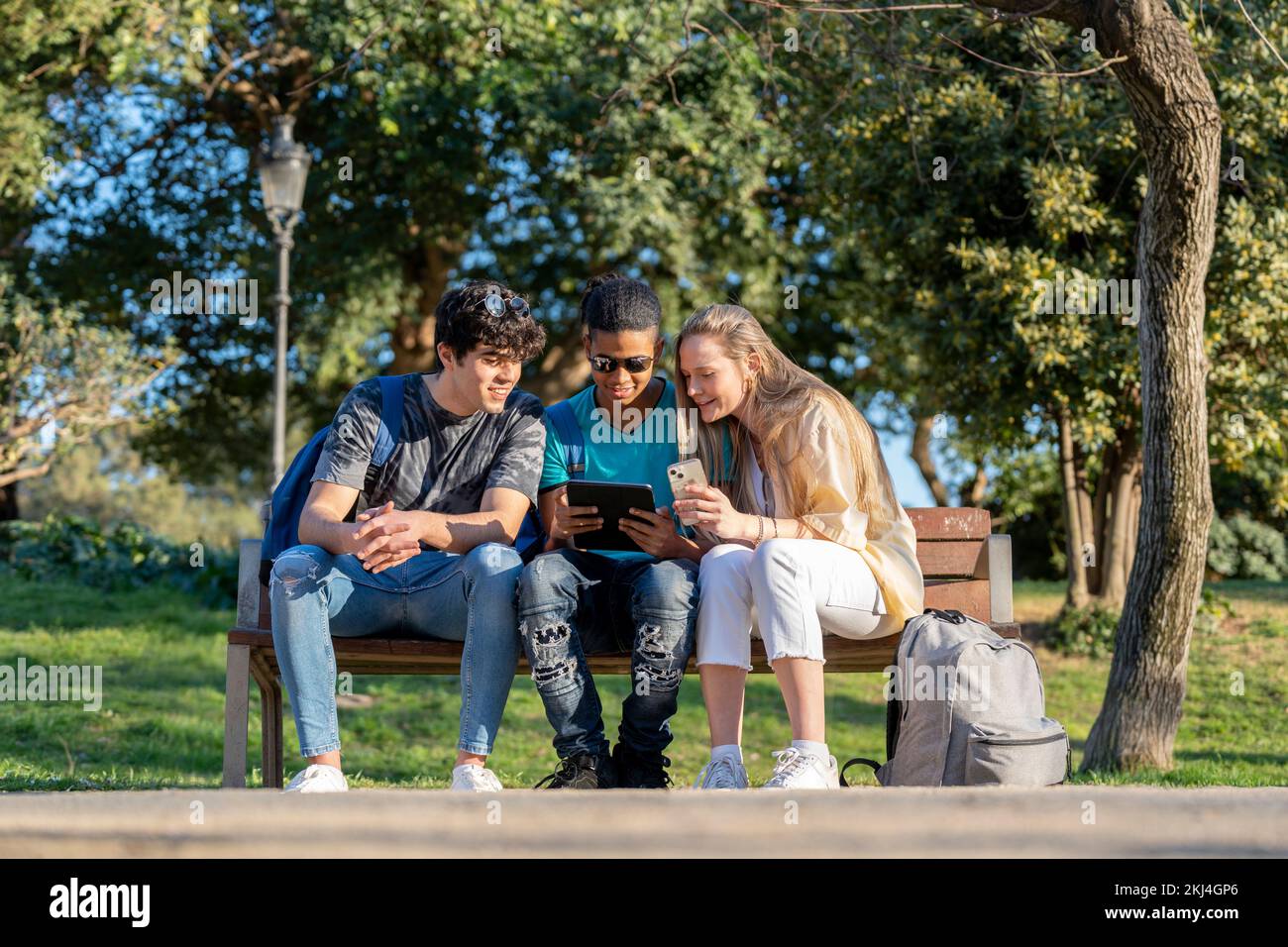 Group of teenage friends looking at a tablet in the park sitting on a ...