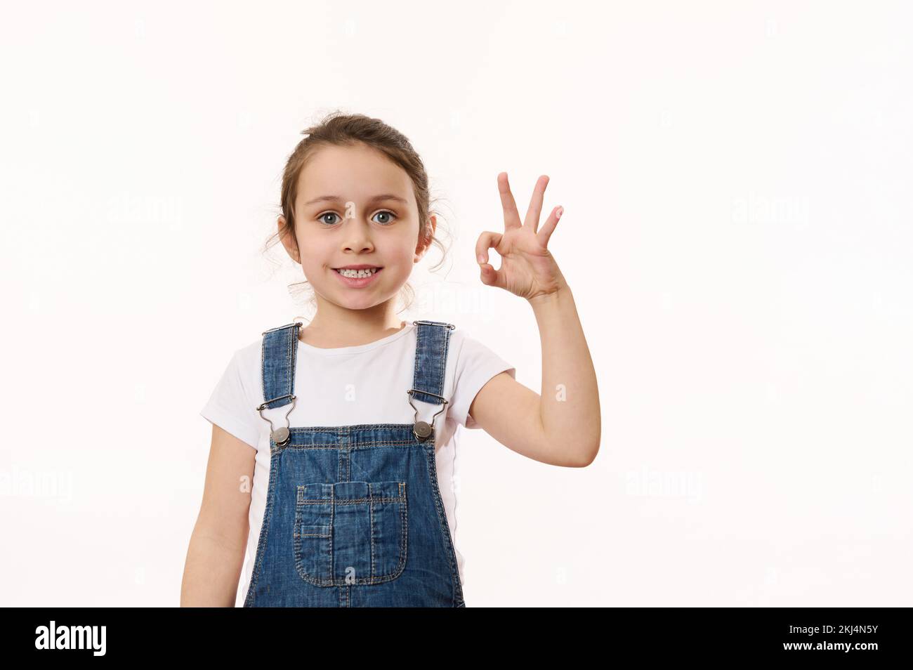 Adorable little girl, in blue denim overalls, gestures, shows peace ...