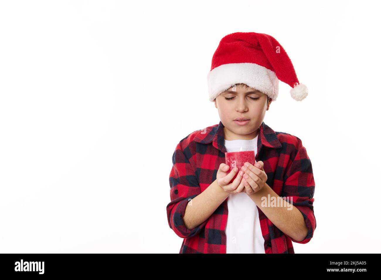 Portrait of a happy child boy in Santa hat, holding a red lit candle ...