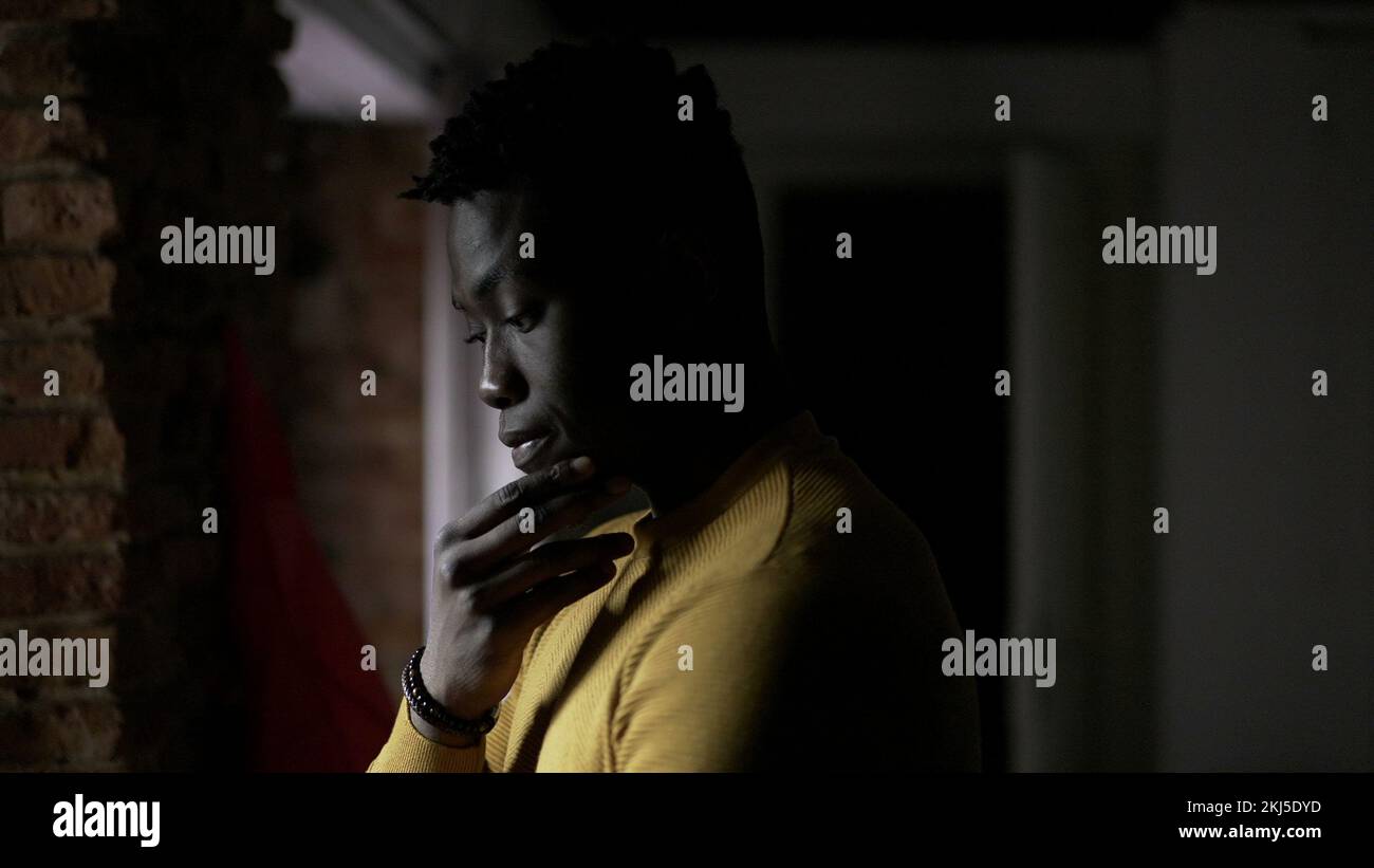 African man standing by window thinking about life. Concerned worried ...