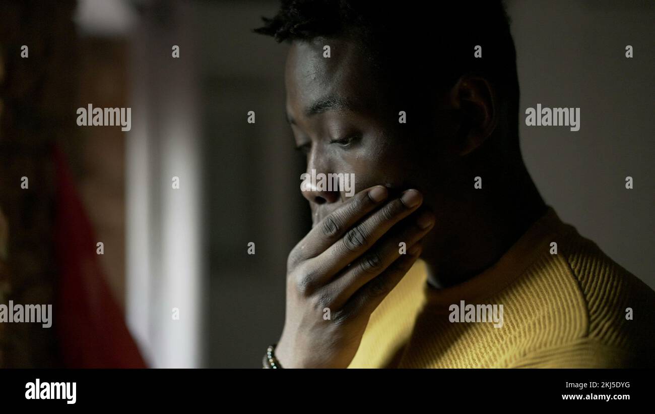 African man standing by window thinking about life. Concerned worried ...