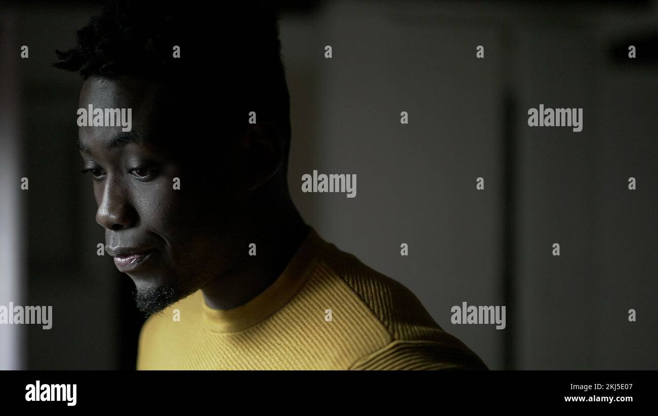 African man standing by window thinking about life. Concerned worried ...